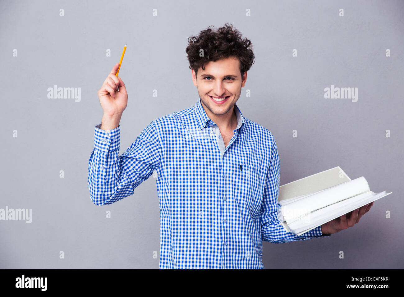 Happy casual man holding pencil and folder with files over gray ...