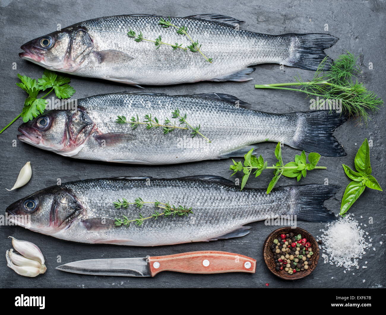 Three fish - seabass on a graphite board with spices and herbs Stock ...