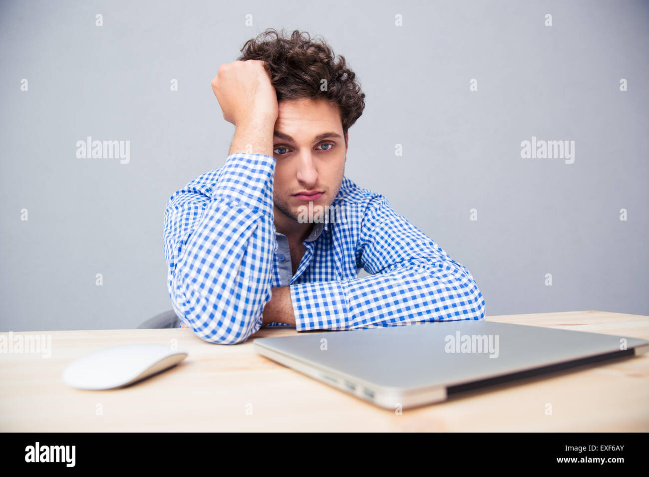 Pensive sad man sitting at the table with laptop over gray background ...