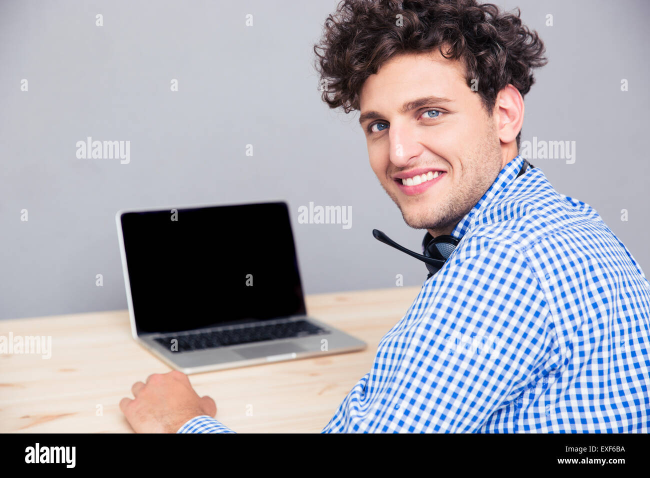 Portrait of a smiling man sitting at the table with laptop and looking ...