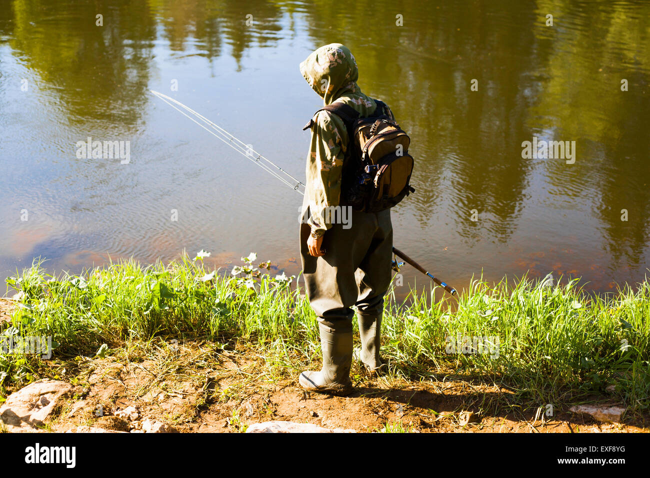Rear view of mid adult man fishing from riverbank, Sarsy village ...