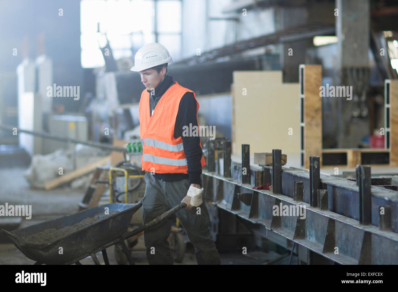 Factory worker pushing wheelbarrow in concrete reinforcement factory ...