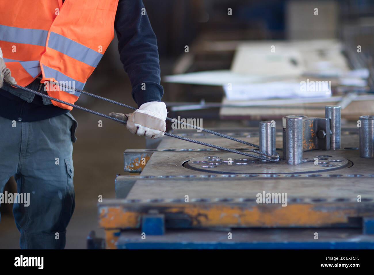 Factory worker bending metal rod in concrete reinforcement factory ...