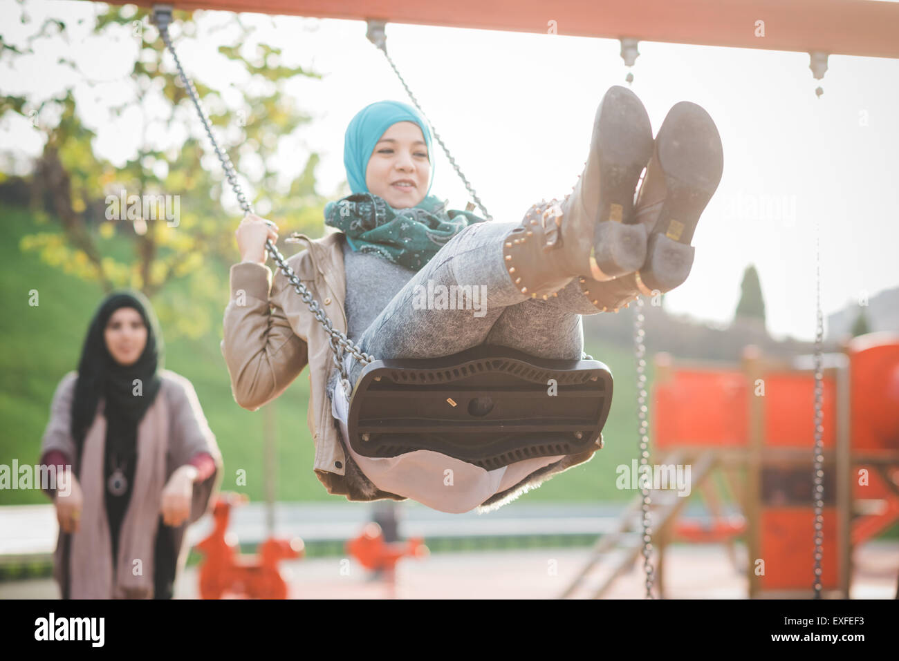 Two young women playing on playground swings Stock Photo - Alamy