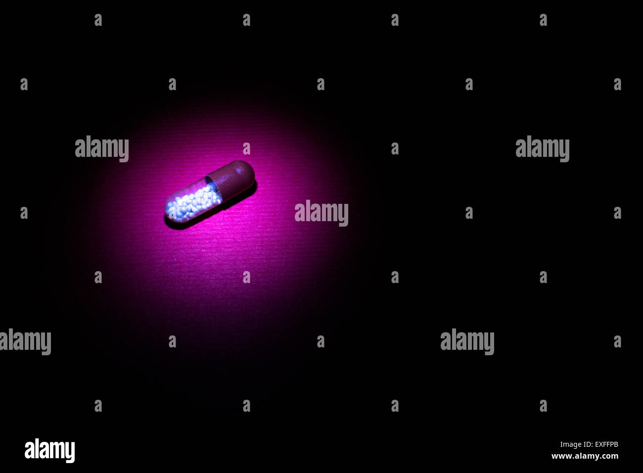 Single pill capsule with contents in light area amongst darkness on a ...