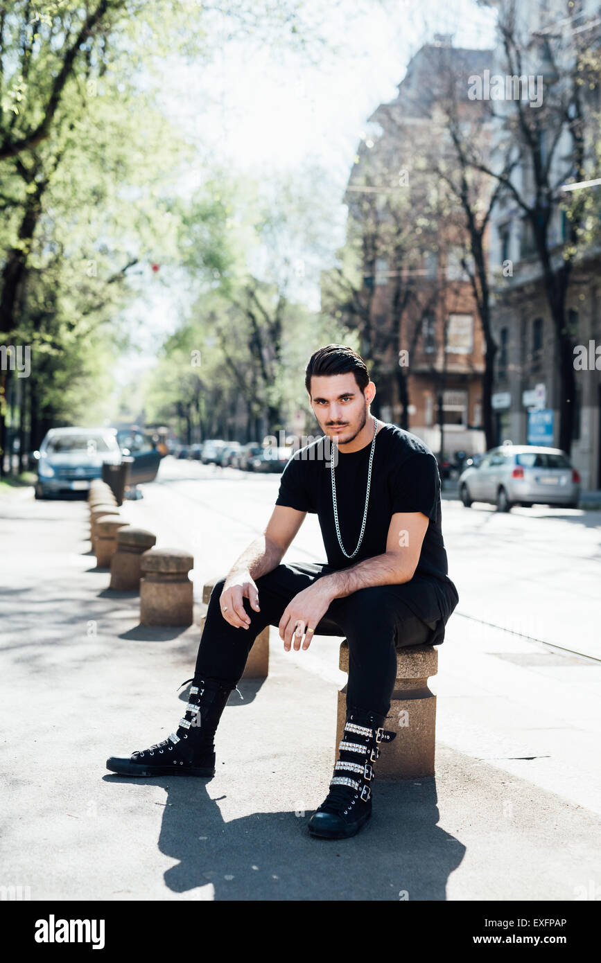Young handsome italian boy seated on sidewalk in the street posing ...