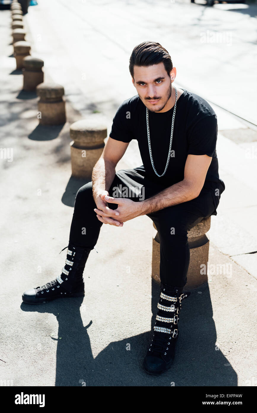 Young handsome italian boy seated on sidewalk in the street posing ...
