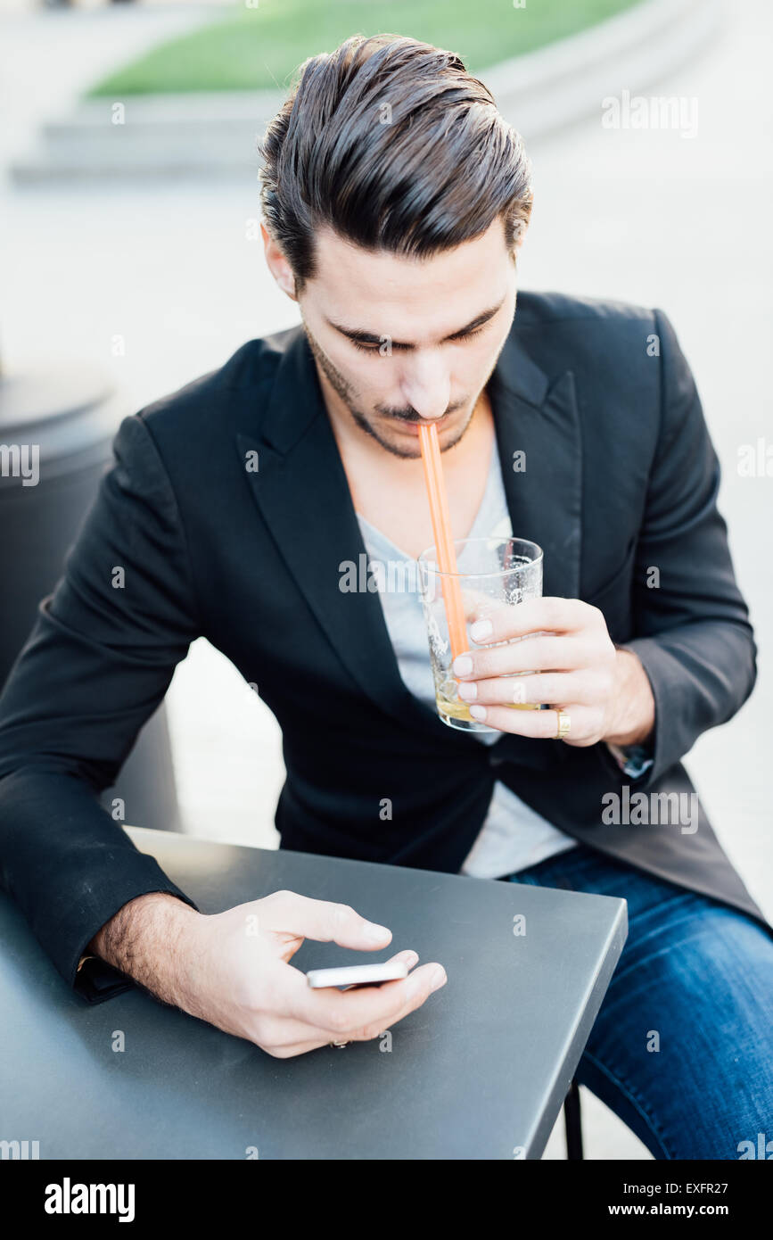 Young handsome italian boy seated on a bar in the city drinking a juice ...