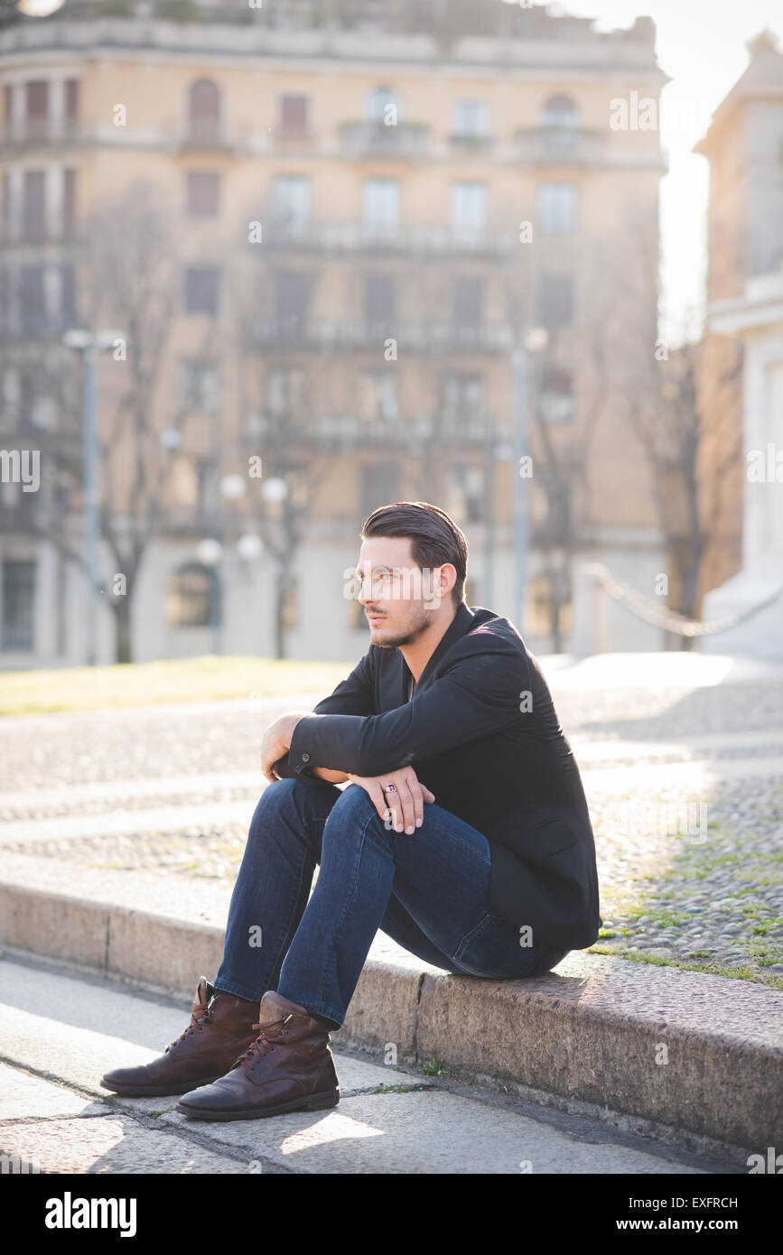 A young handsome italian boy seated on a sidewalk in the city center ...
