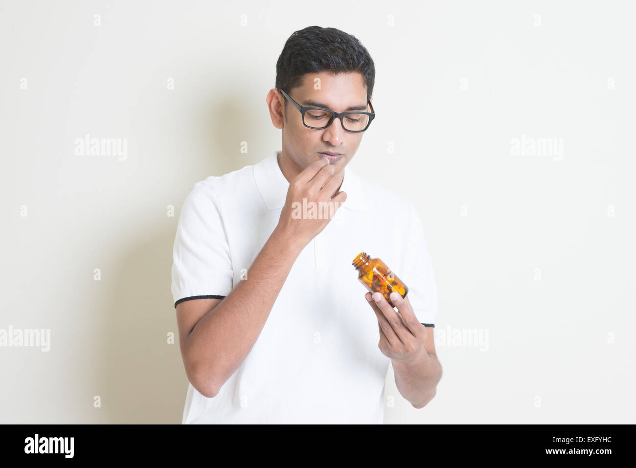 Sick Indian guy eating medicine pill. Asian man standing on plain ...