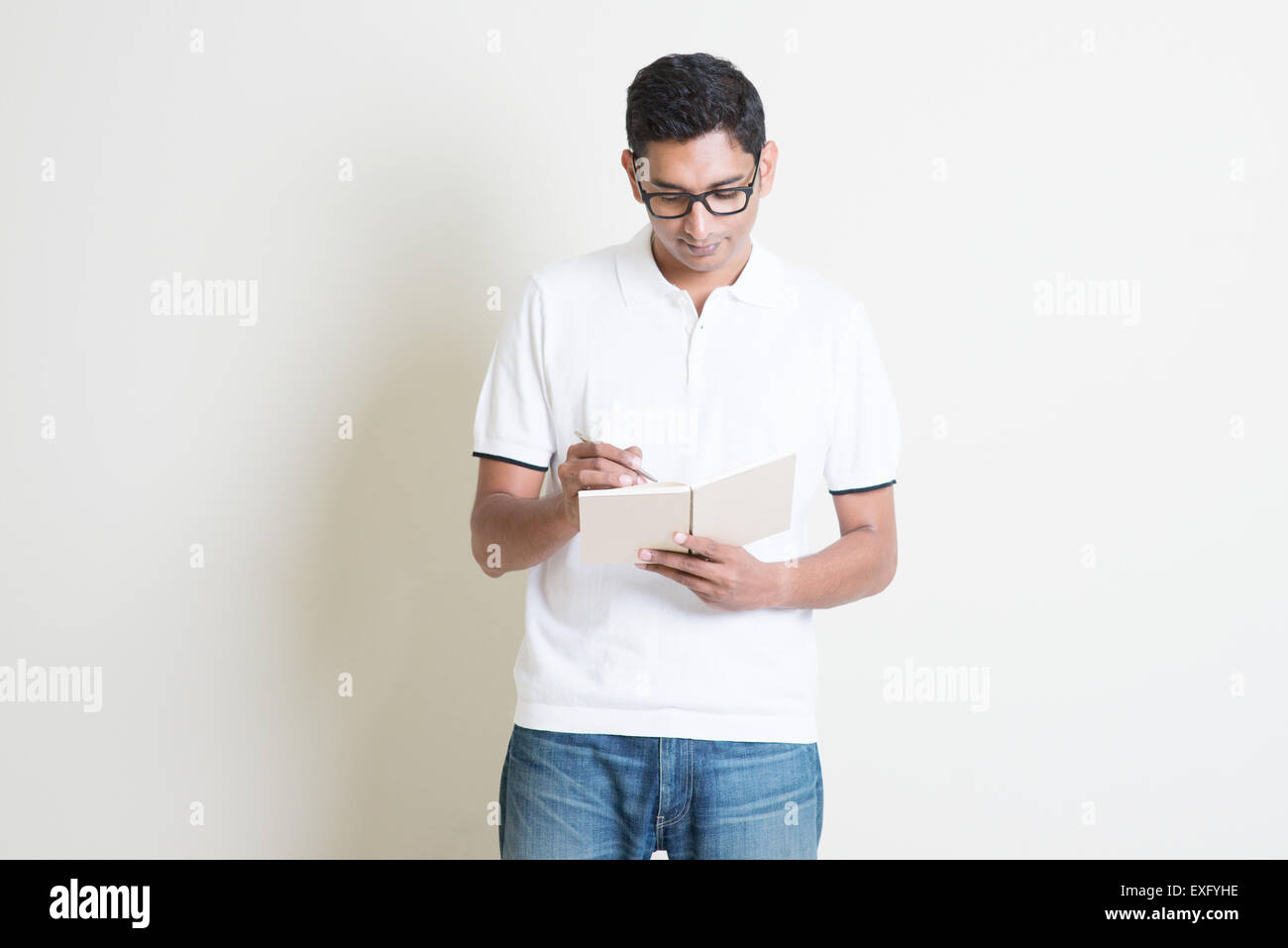Portrait of Indian guy taking note on book. Asian man standing on plain ...