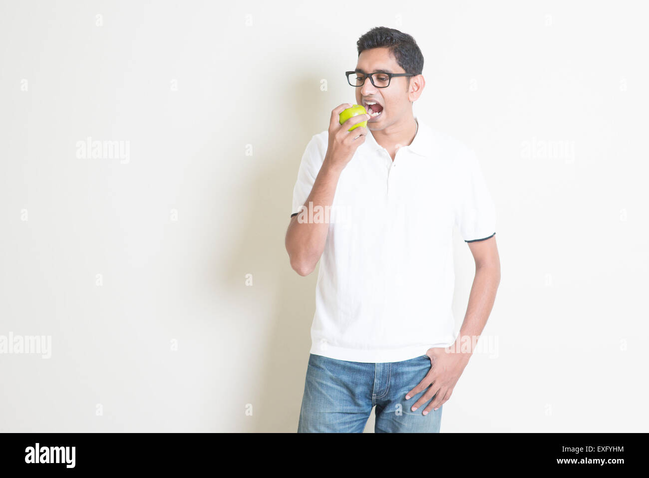 Man healthcare concept. Indian guy eating a green apple. Asian standing ...