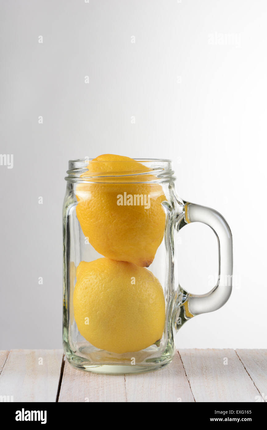 A still life with two lemons in a mason style jar with handle. The ...