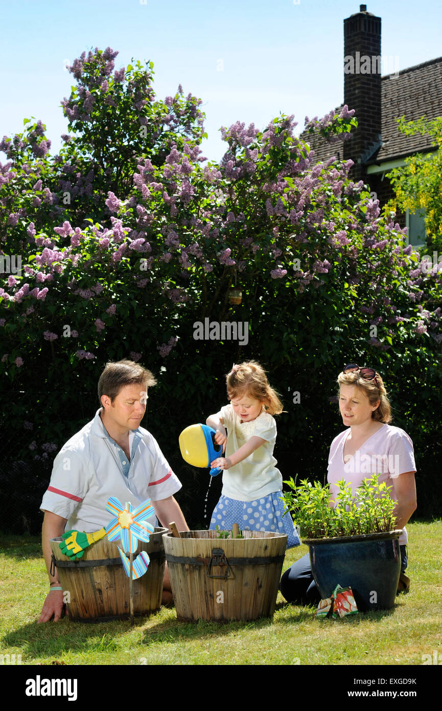 A family with young daughter planting seeds in their back garden ...