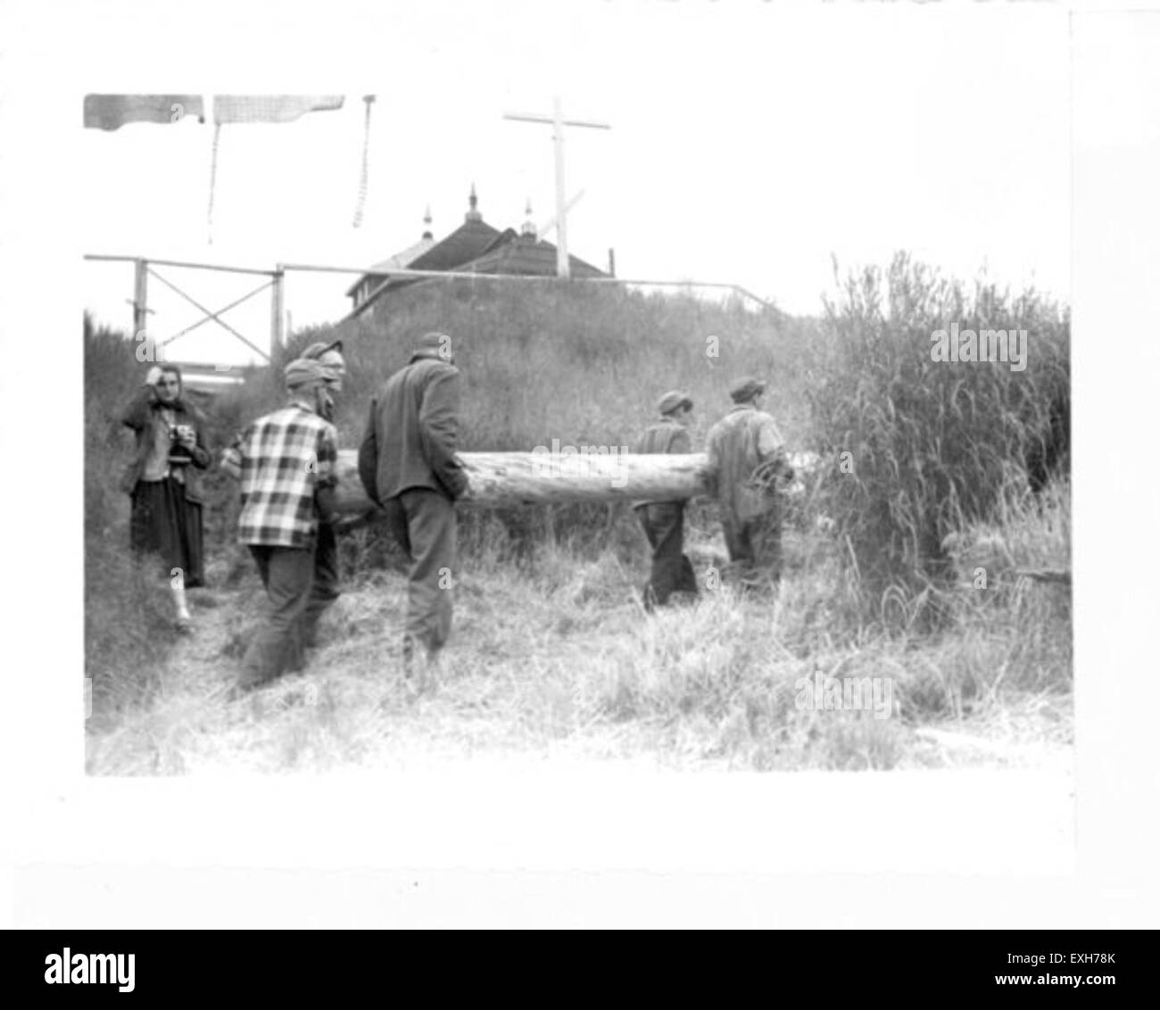 A group of workers is shown carrying logs for a building project ...
