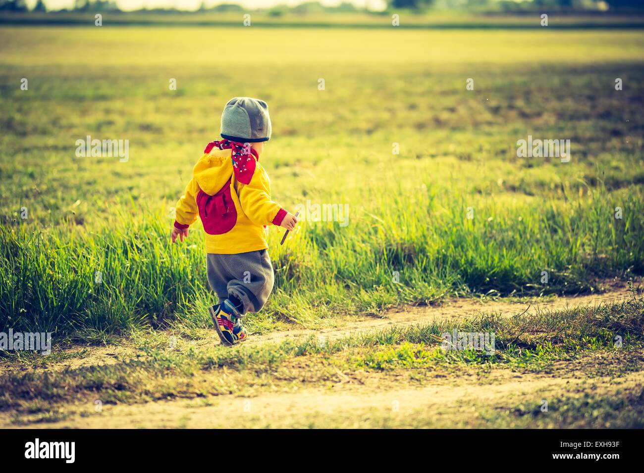 Vintage photo of small child playing on meadow. Beautiful landscape ...