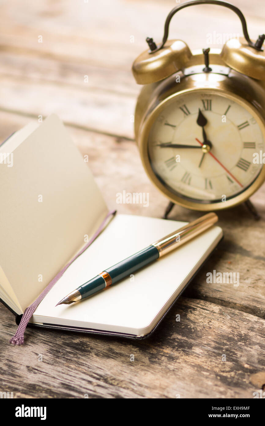 Open small notebook with retro-fashioned fountain pen and alarm clock ...