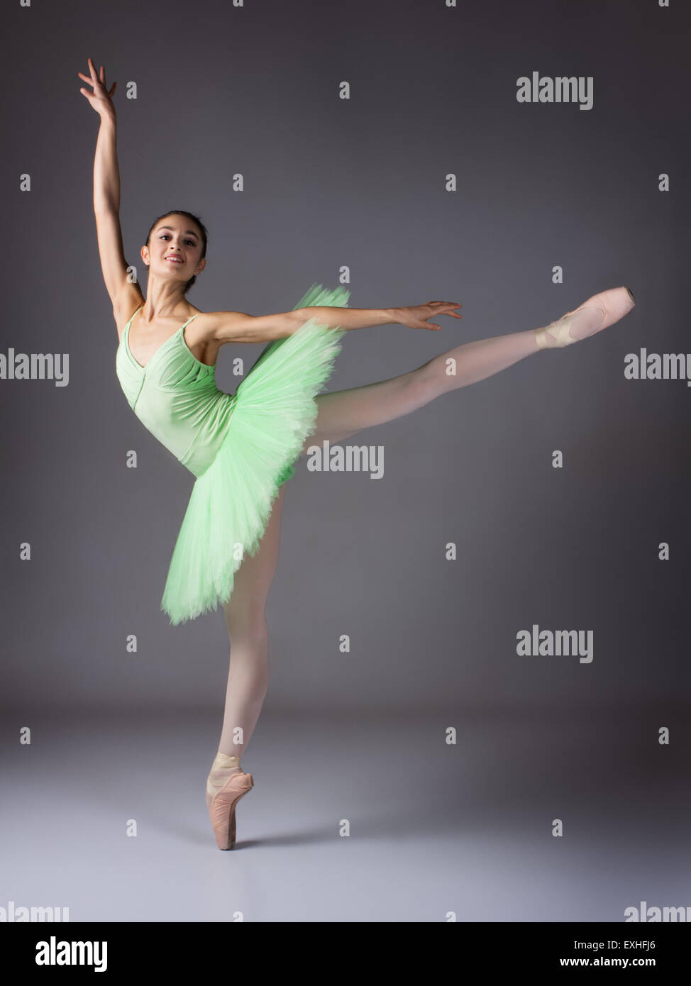 Beautiful female ballet dancer on a grey background. Ballerina is wearing a green tutu and ...