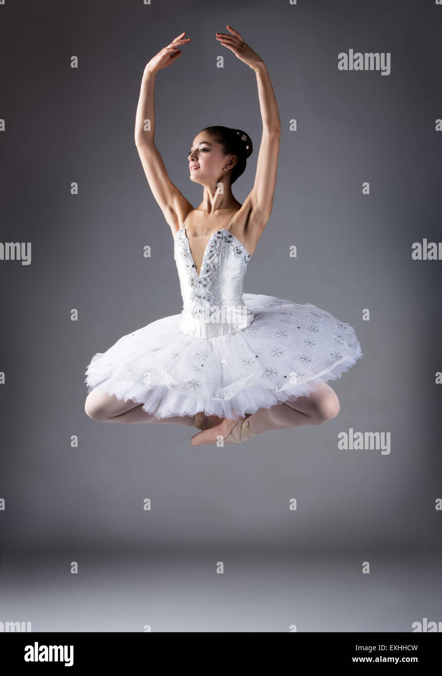 Beautiful female ballet dancer on a grey background. Ballerina is wearing a white tutu and ...