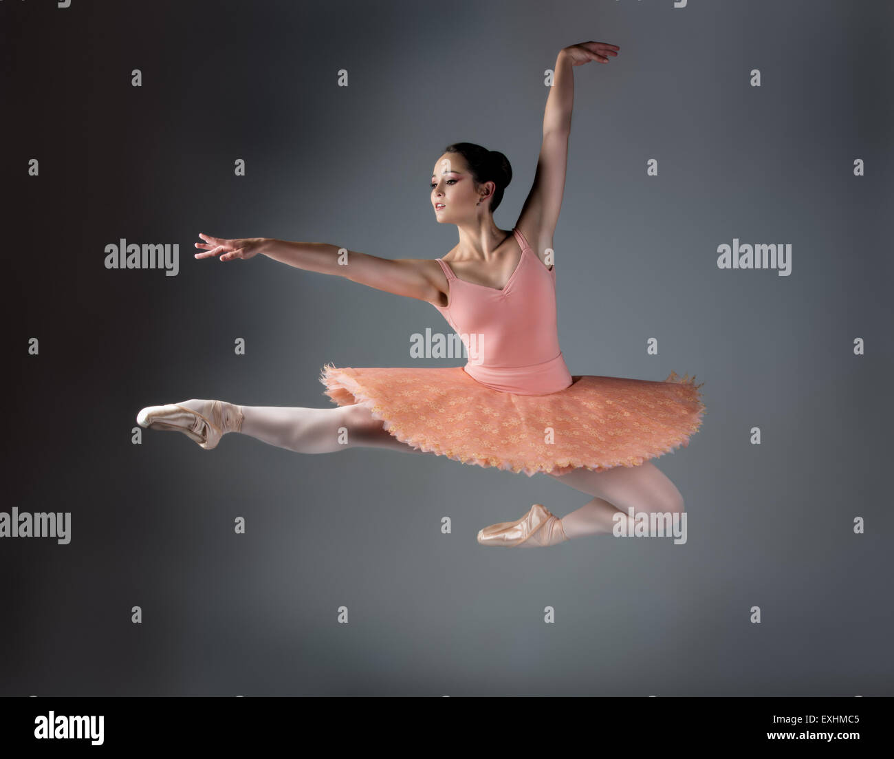 Beautiful female ballet dancer on a grey background. Ballerina is wearing an orange tutu, pink ...