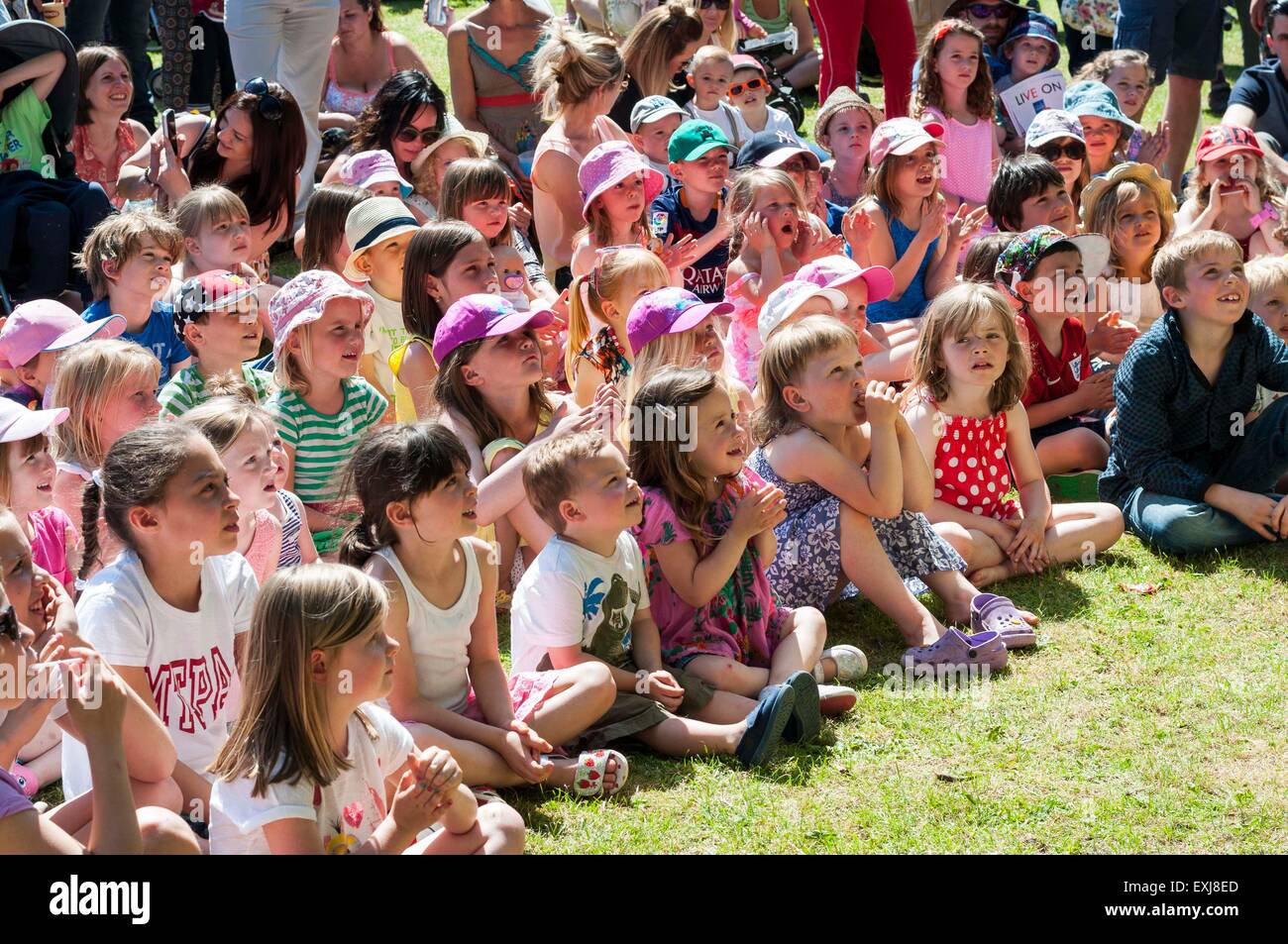 Audience of children sat on the grass in the sunshine watching a Punch ...