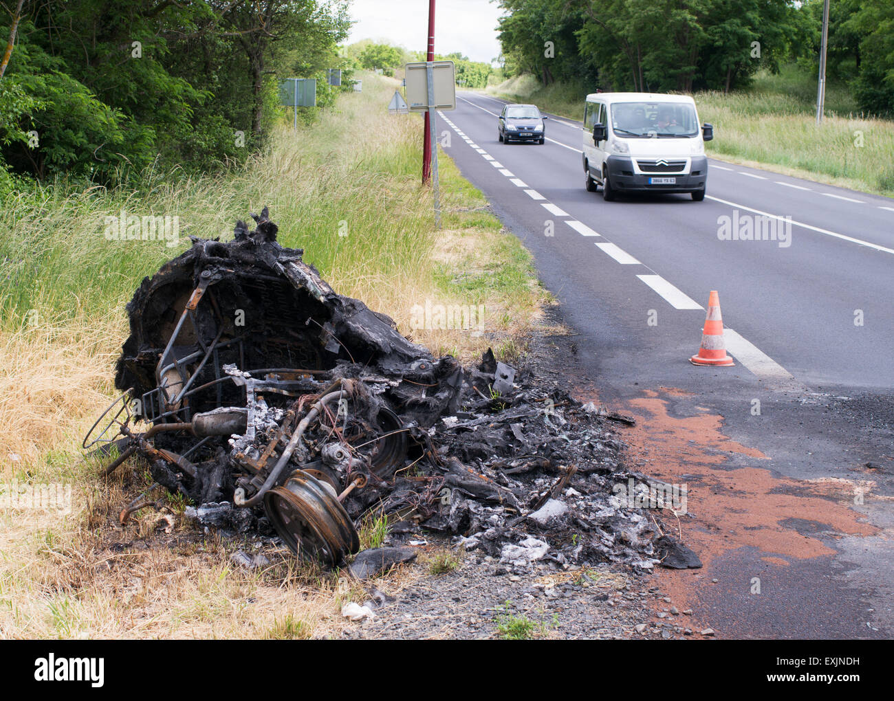 The burnt out remains of a road vehicle at the side of a road in France ...
