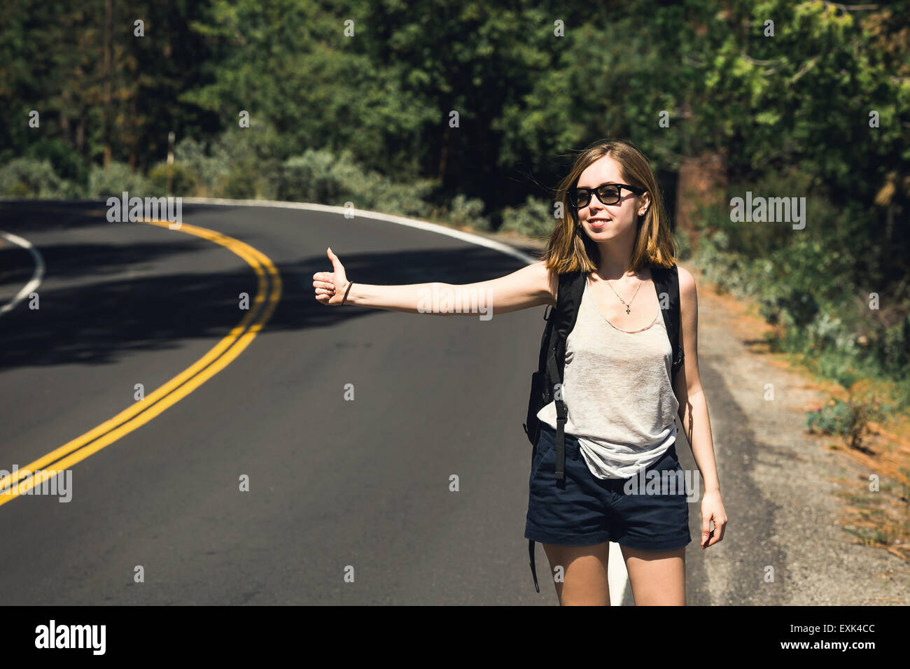 Hitchhiker Woman Hitch A Lift With A Thumbing Hand Up Walking On A Roadside Of A Highway While