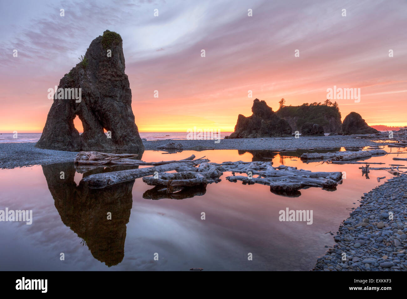 Sunset reflected in a slow moving stream, with sea stacks and driftwood ...