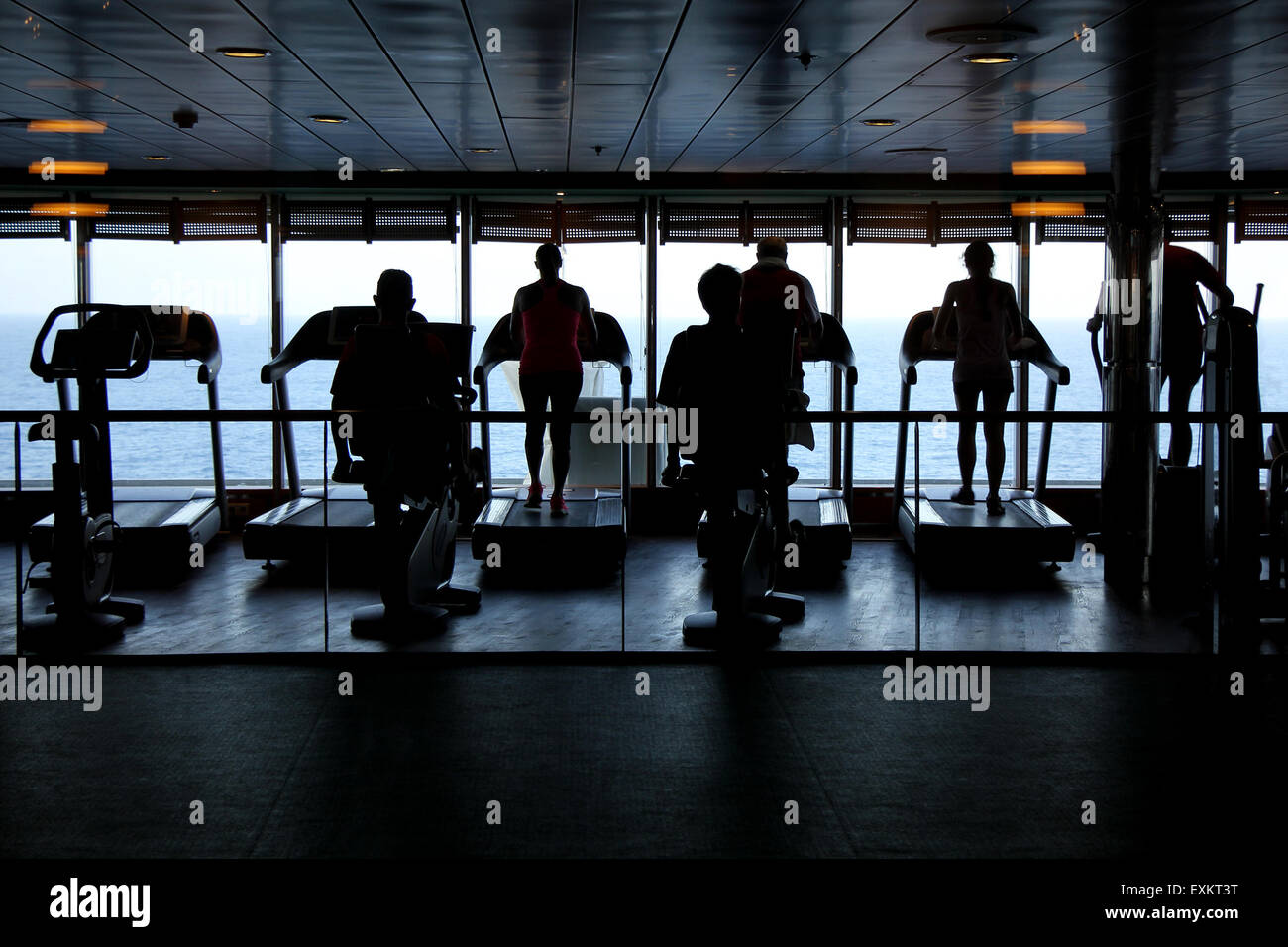 People exercising at the gym on a cruise ship in silhouette on sea ...