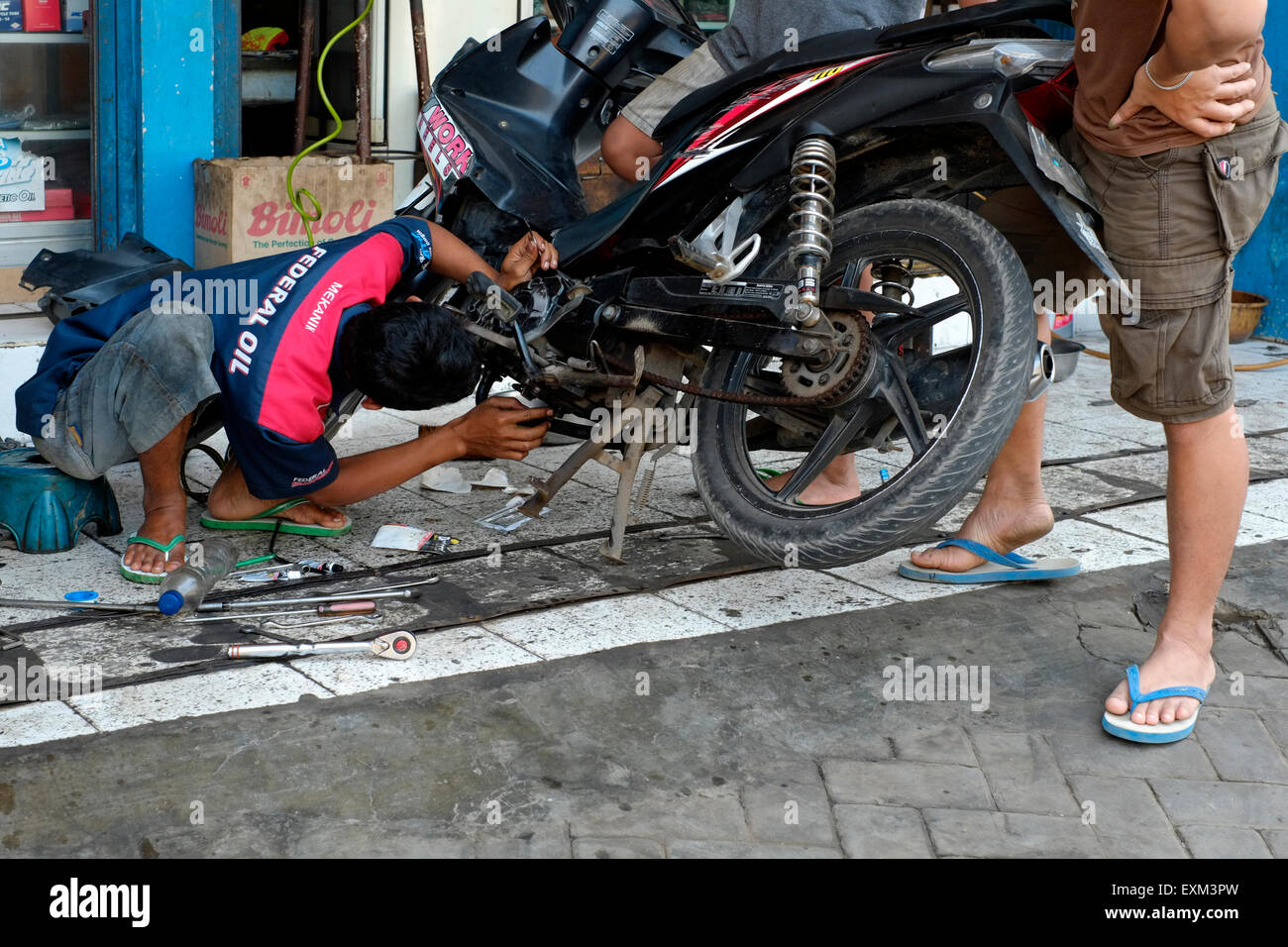 local male mechanic fixing a problem on a moped as the owners look on ...