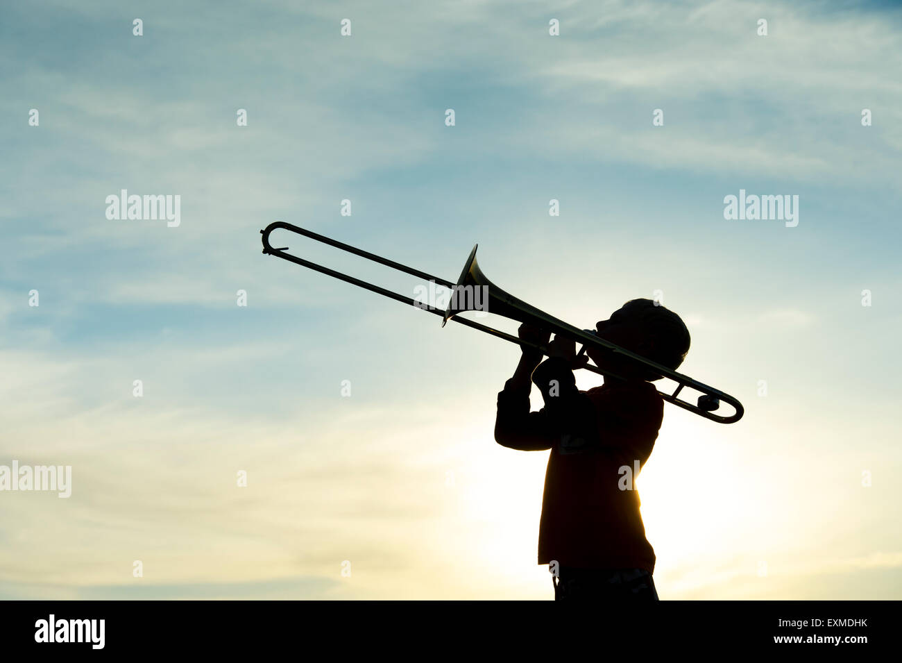 Silhouette of young boy playing a trombone against a sunset background ...