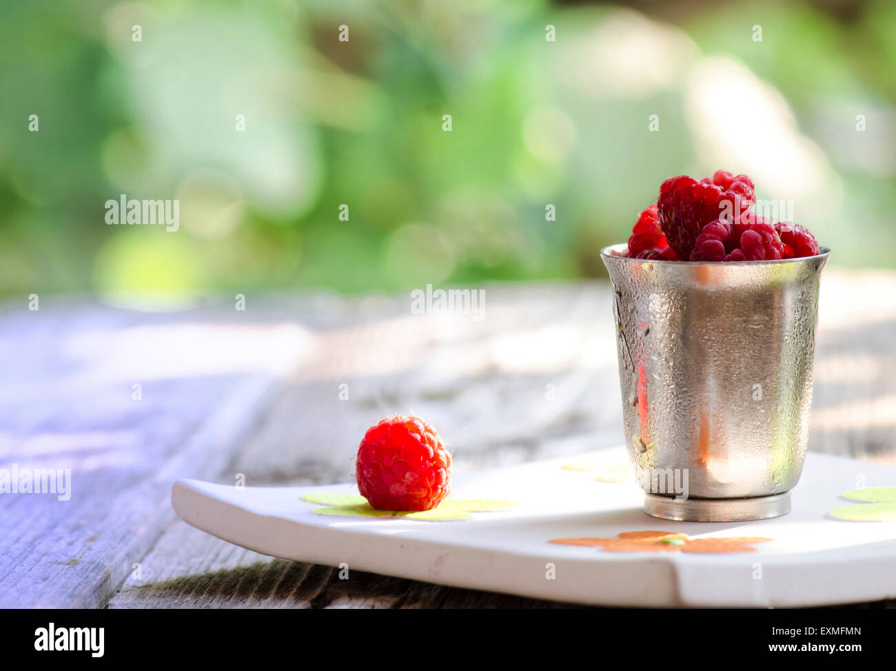 Raspberries in a cup and on a white flowered plate on vintage wooden ...