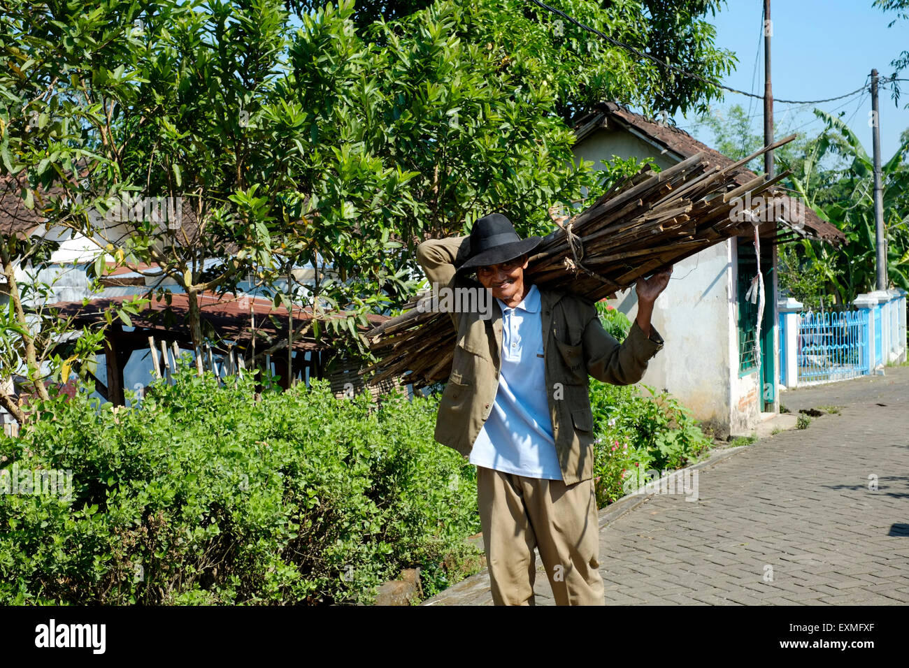 smiling villager carrying bundle of sticks in a rural village street in ...