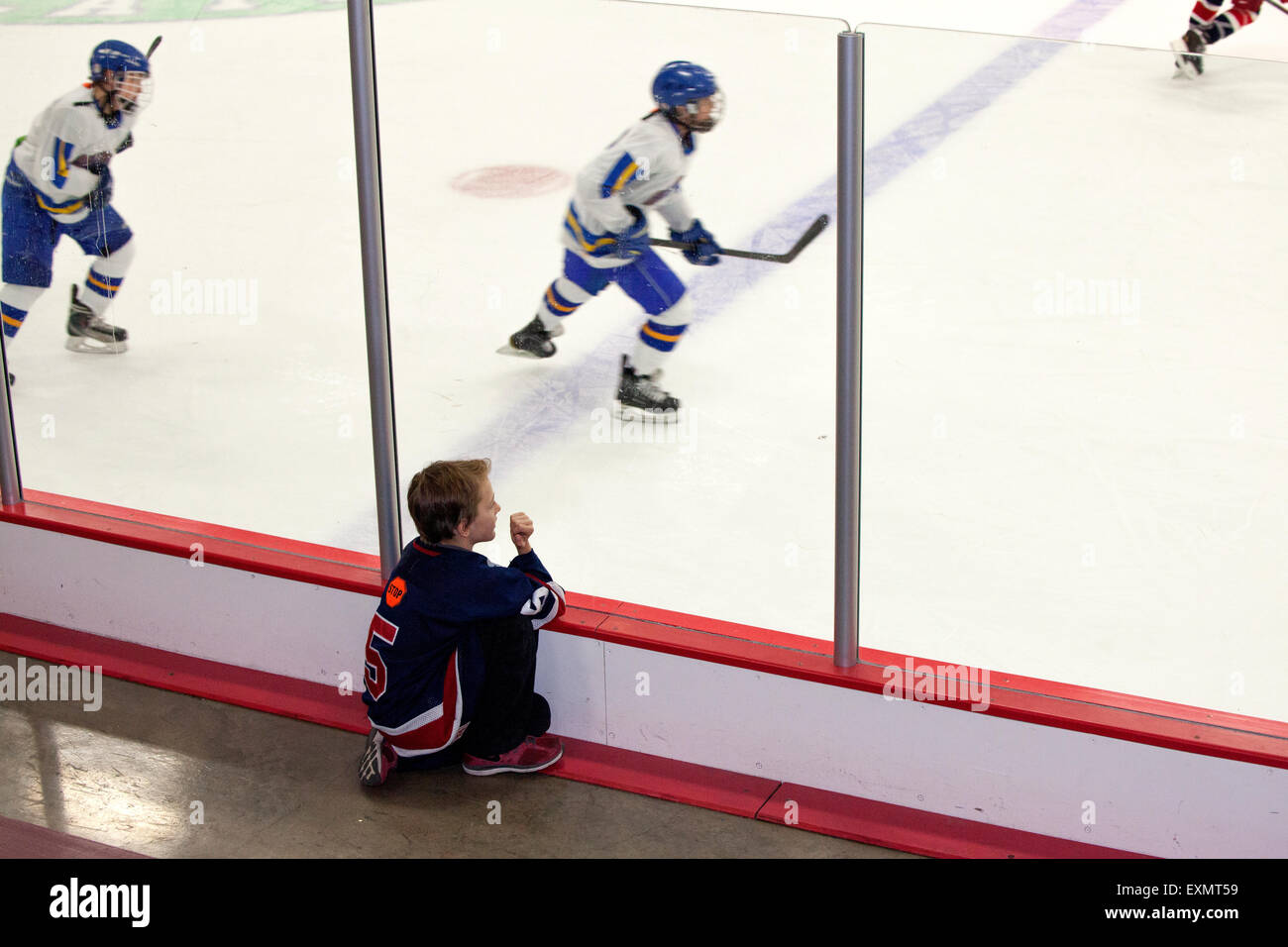 Young boy intensely watching indoor hockey game behind plastic window ...