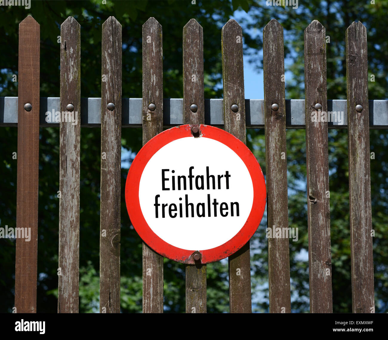Round German sign on a wooden fence instructs "Keep entrance clear ...