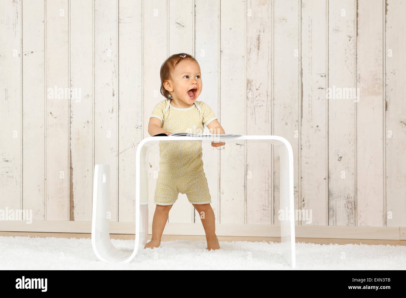 Baby girl standing behind modern side table Stock Photo - Alamy