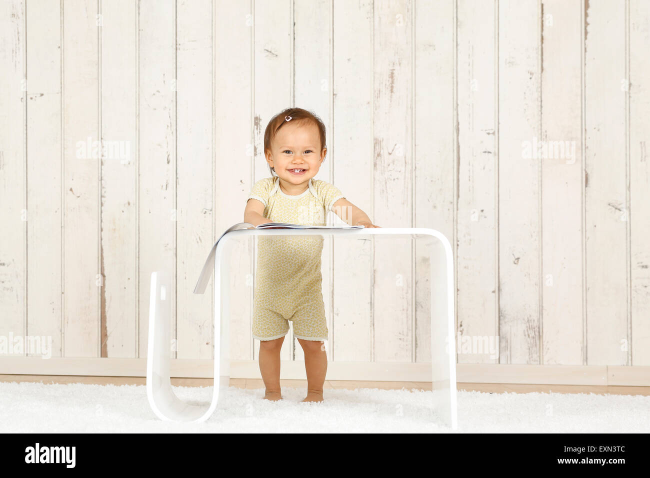 Smiling baby girl standing behind modern side table Stock Photo - Alamy