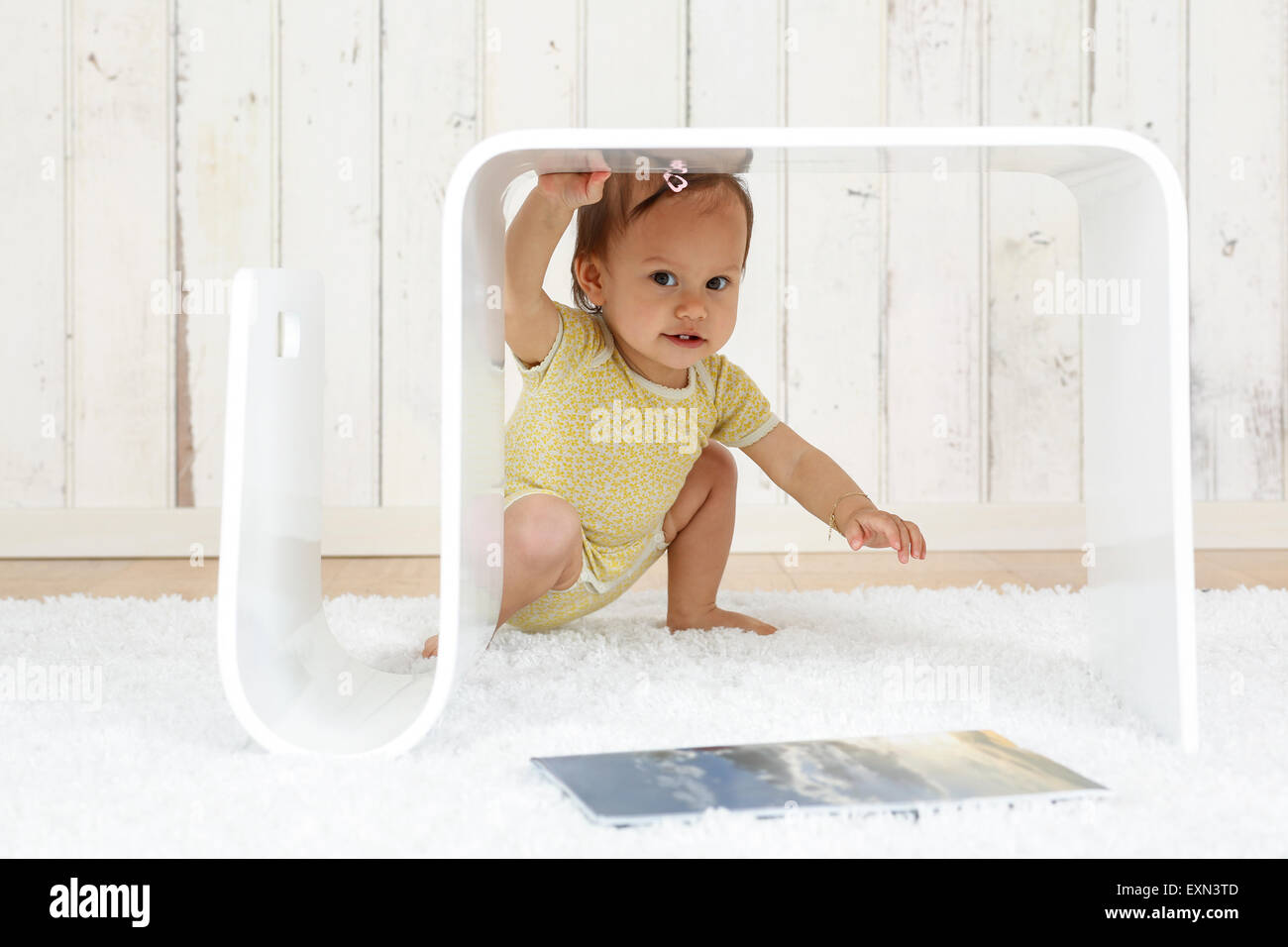 Baby girl crouching under modern side table Stock Photo - Alamy
