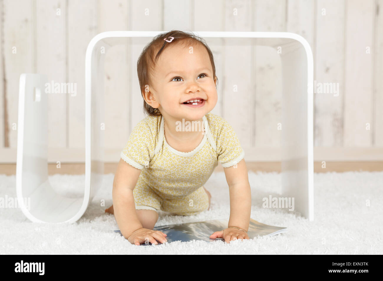 Portrait of smiling baby girl crouching under modern side table Stock ...