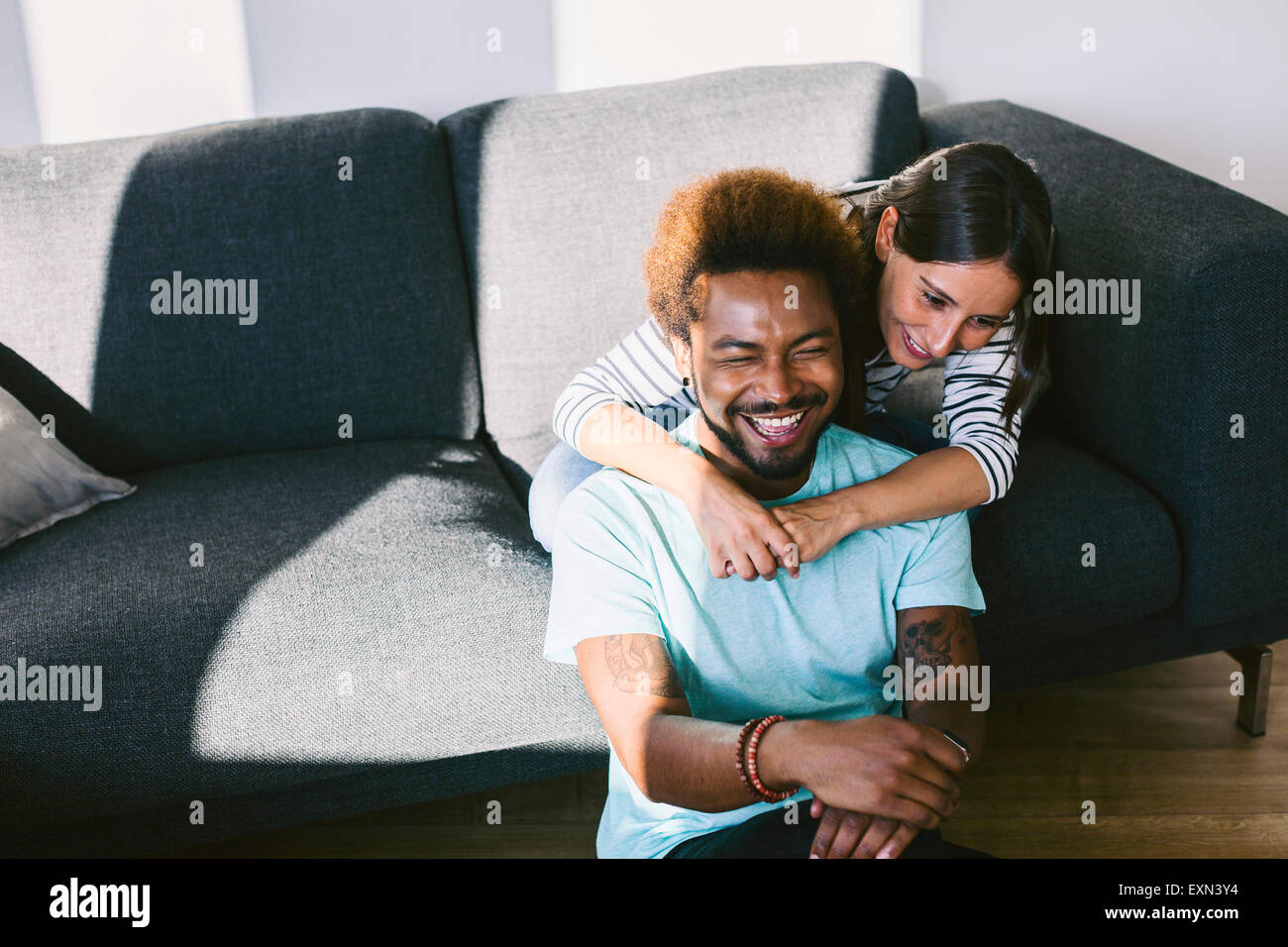 Happy young couple sitting on couch with arms around Stock Photo - Alamy