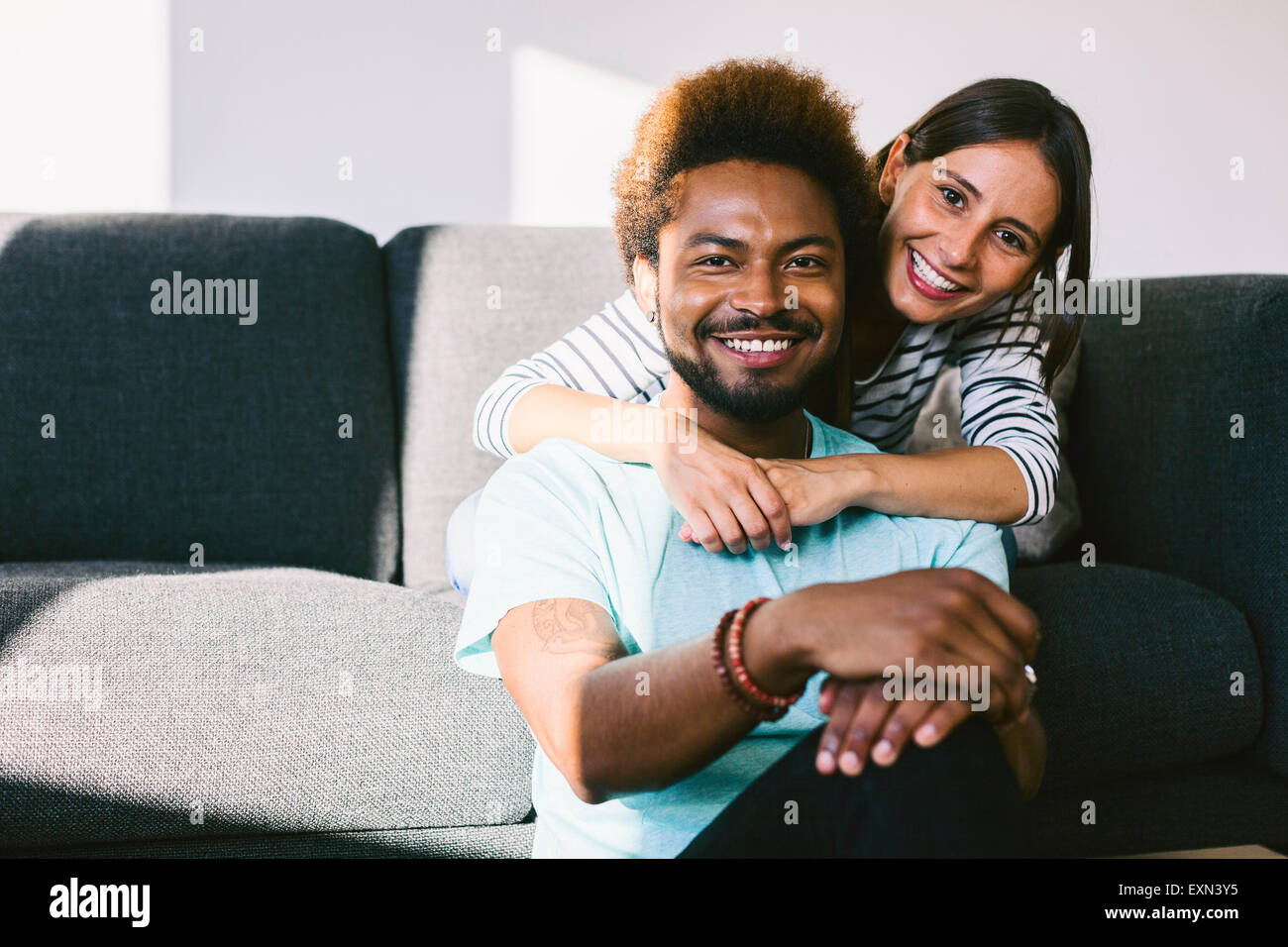 Happy young couple sitting on couch with arms around Stock Photo - Alamy