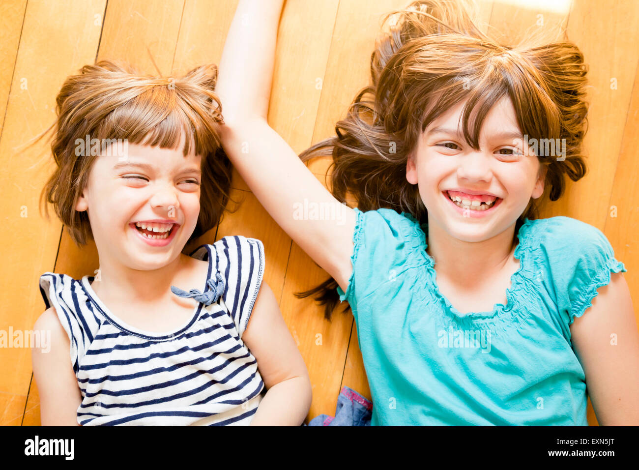 Portrait of two laughing sisters lying on wooden floor Stock Photo - Alamy