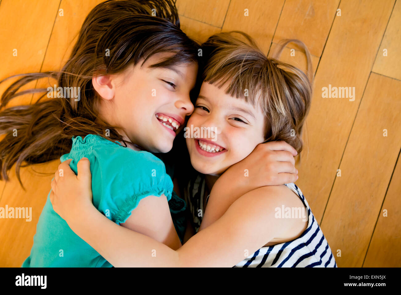 Two happy sisters hugging on wooden floor Stock Photo - Alamy