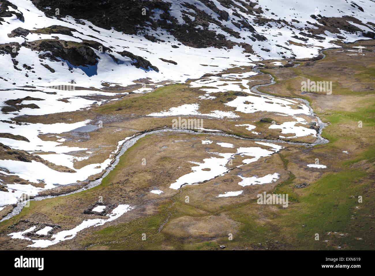 Alpine stream weaves across green valley floor among ruined huts near ...