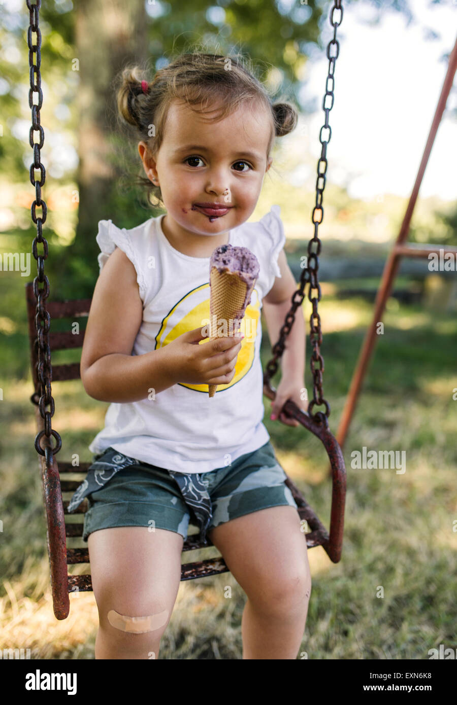 Portrait of happy little girl sitting on a swing eating ice cream Stock ...