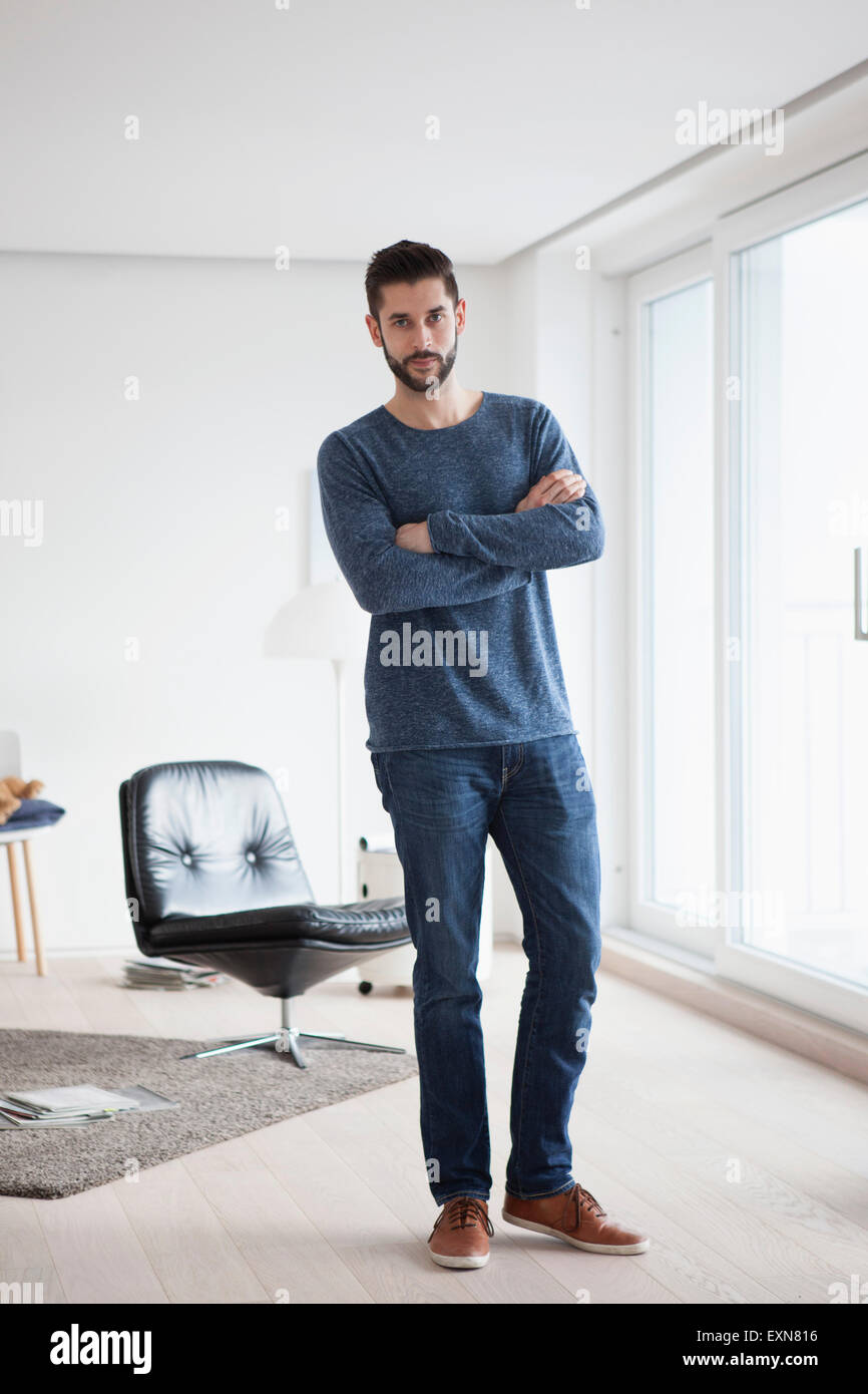 Portrait of young man with crossed arms standing in his living room ...