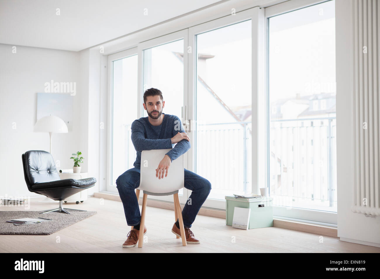 Young man sitting on chair in his living room Stock Photo - Alamy