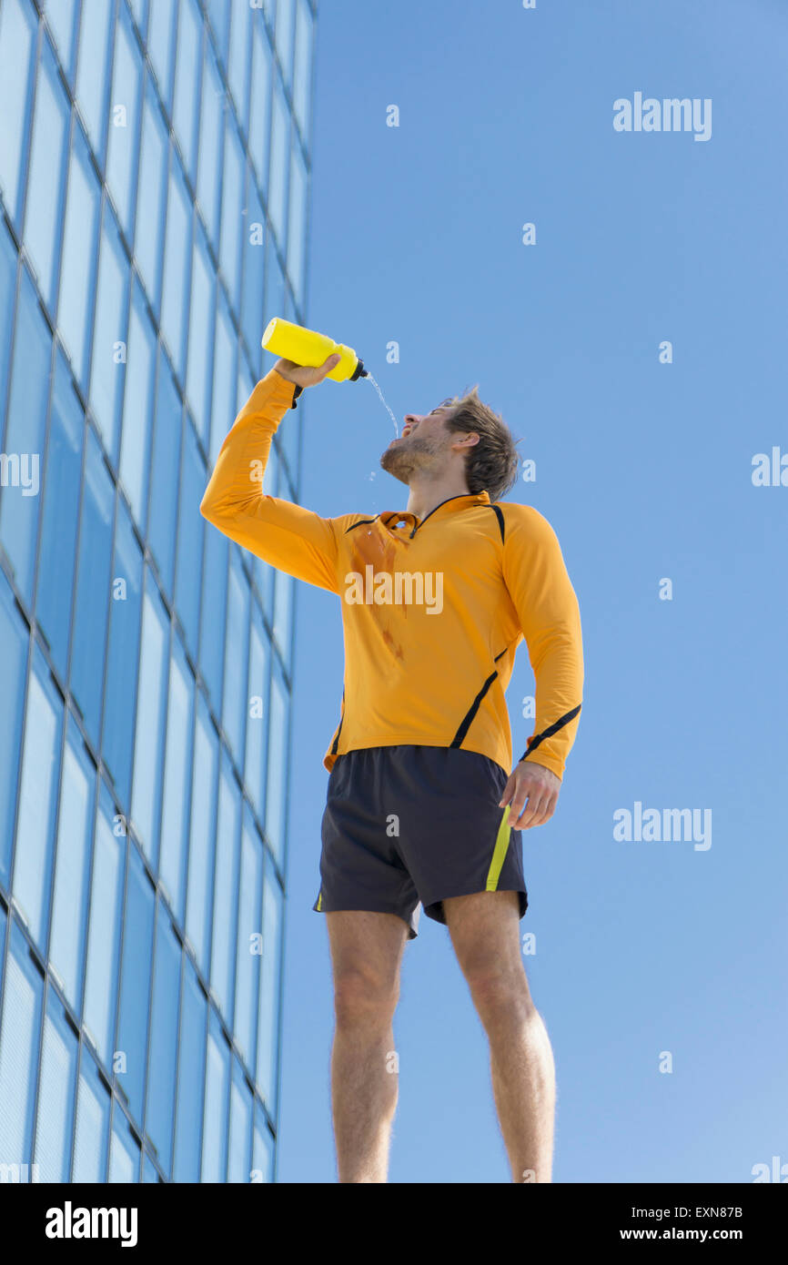 Athlete drinking from bottle at high-rise building Stock Photo - Alamy