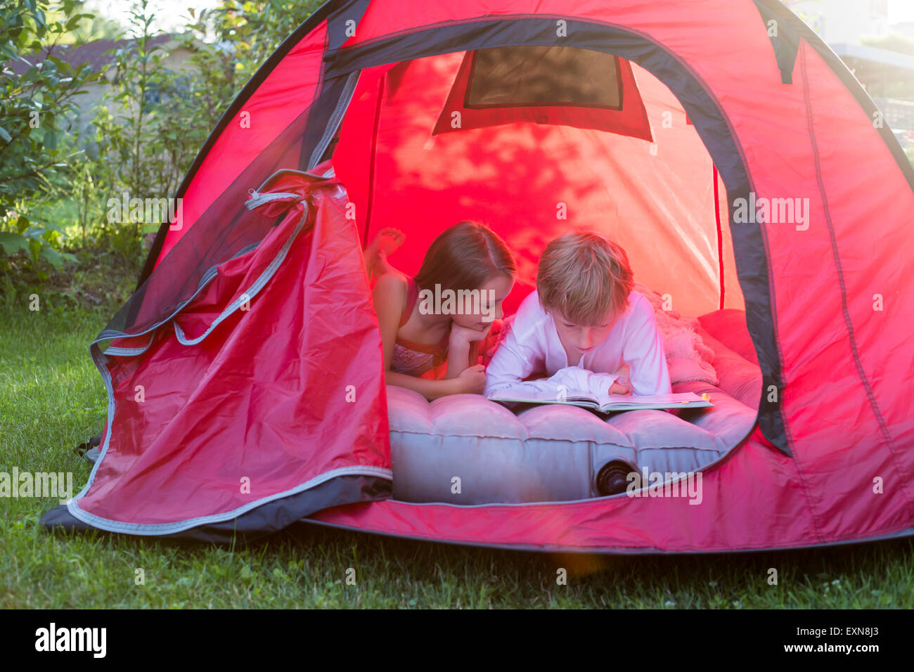 Boy and girl reading lying in a red tent with a book Stock Photo - Alamy