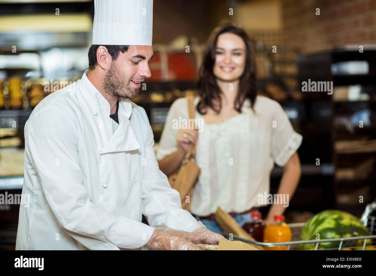 Male chef in bakery helping female client in supermarket Stock Photo ...